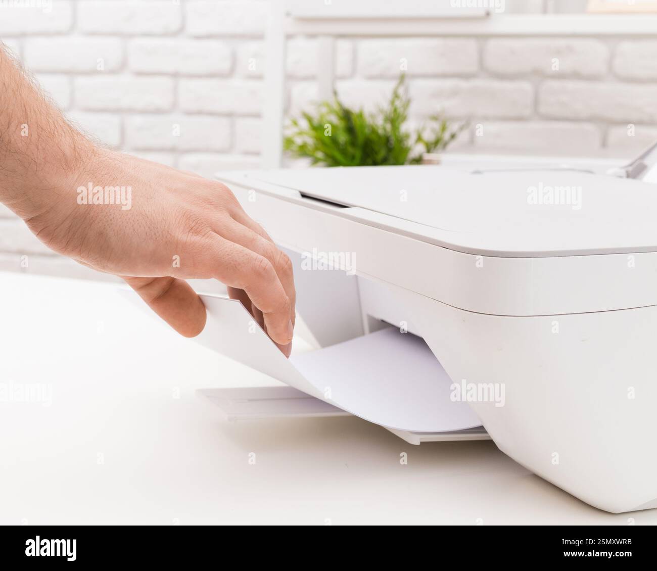 Hand pulling printed paper from a modern printer in a bright workspace ...