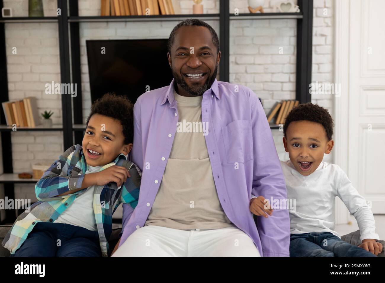 Happy dad sitting with his two sons and looking contented Stock Photo ...