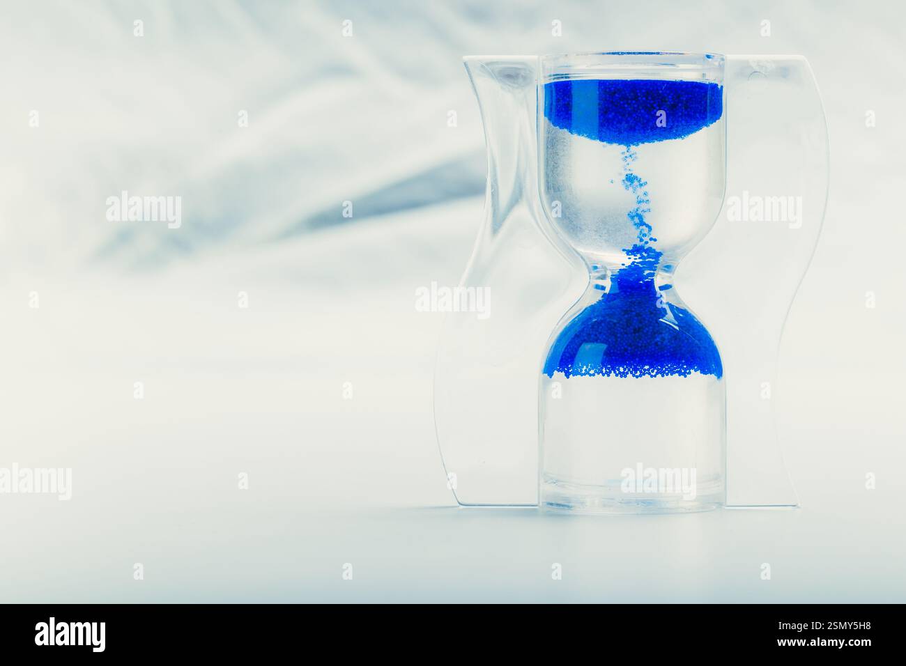 Colorful hourglass with blue sand resting on a light background during ...