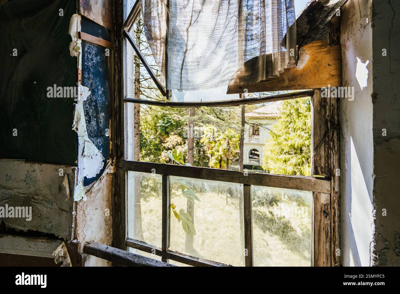 broken window in abandoned building with tattered curtain and view of ...