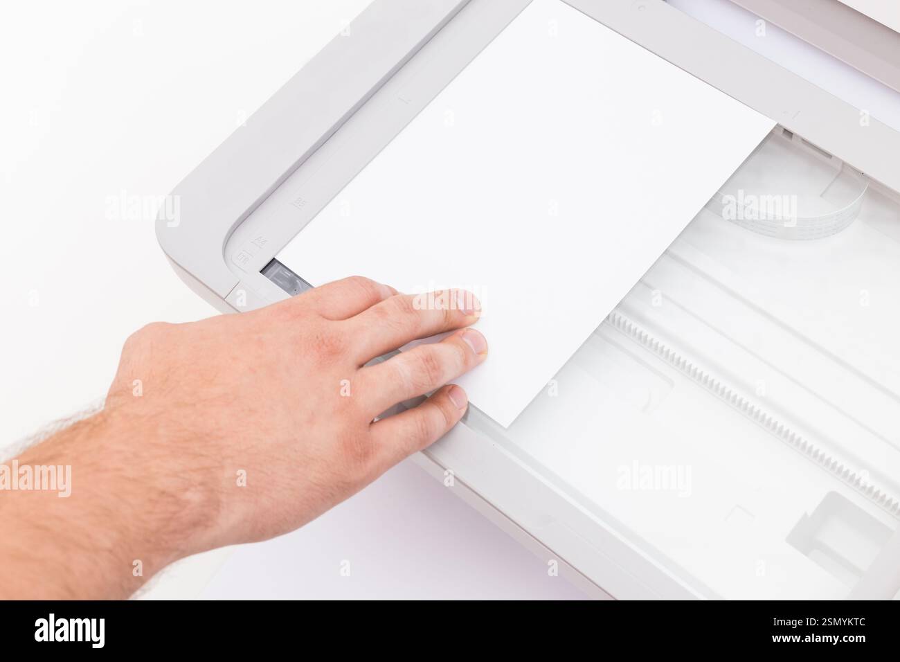 Hand placing a blank sheet of paper into a scanner on a white surface ...