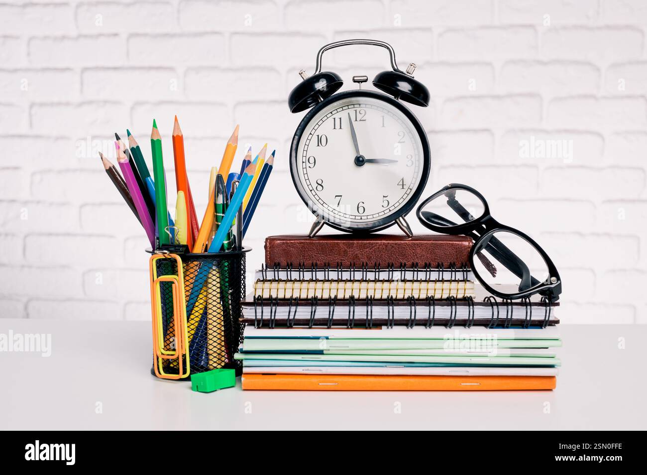 Colorful stationery and clock on a desk with stacked notebooks and ...