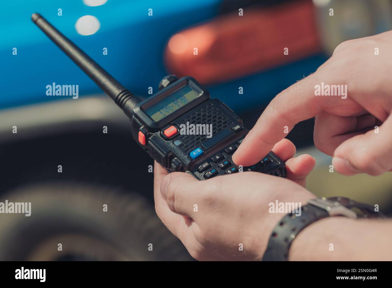Individual operates handheld radio while standing next to blue vehicle ...