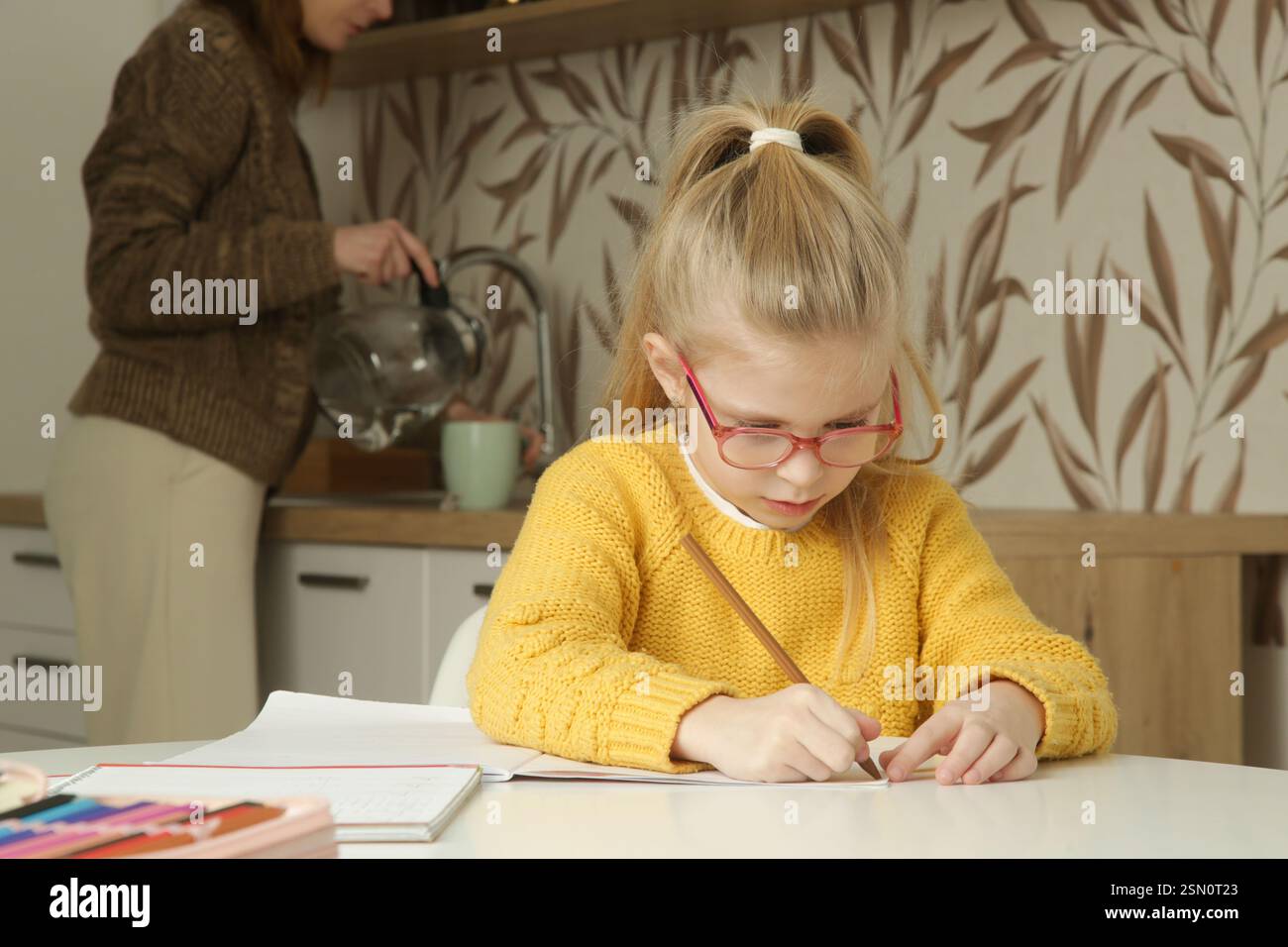 Little girl, elementary school student, doing homework at kitchen table ...