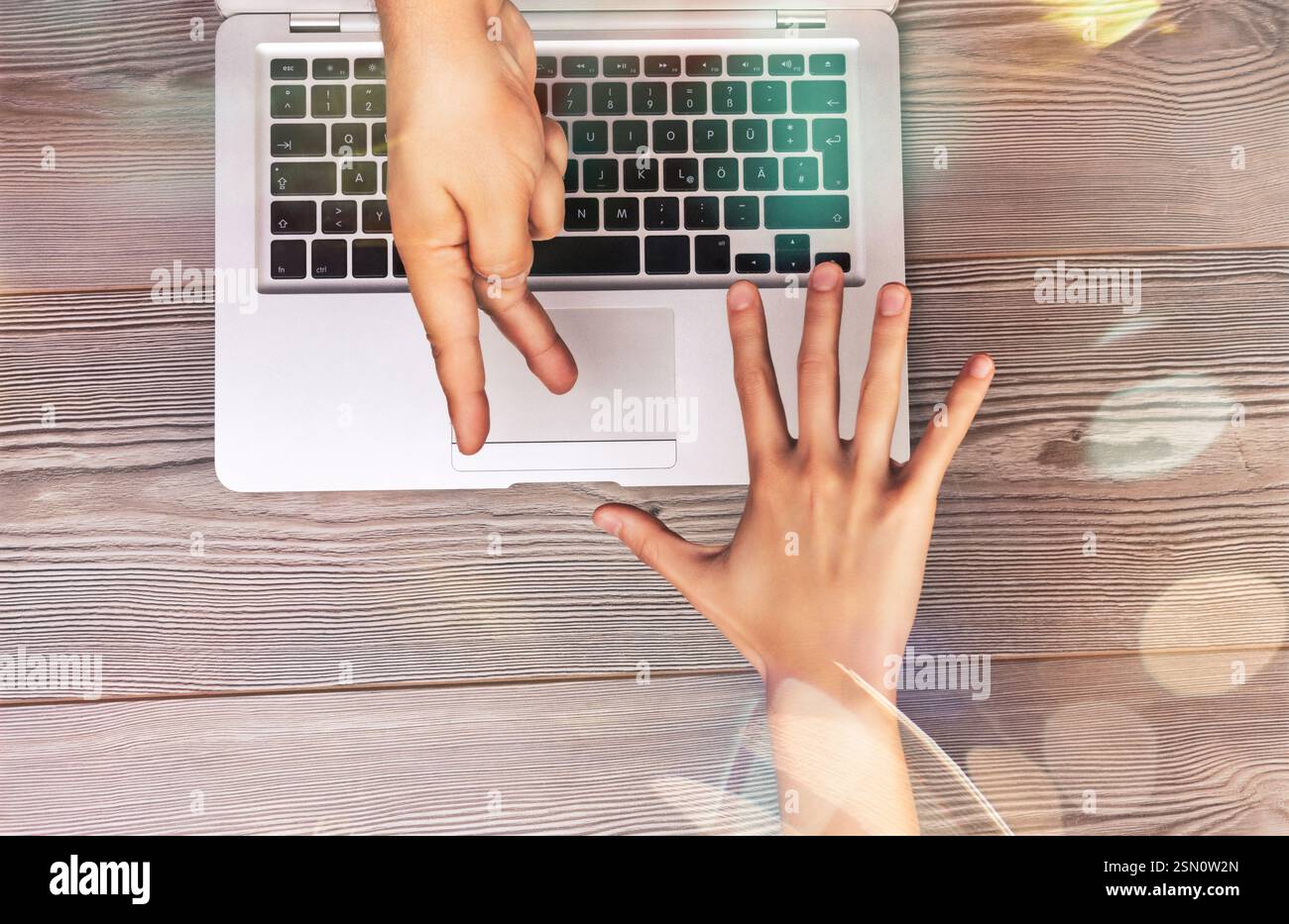 Adult hand guiding child's hand on a laptop keyboard, representing the ...