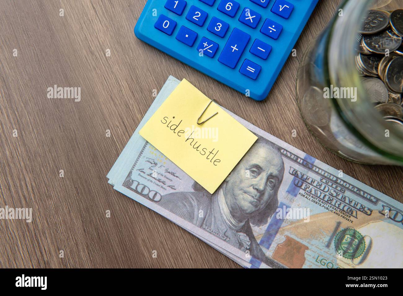 A sticky note with the words "side hustle" on top of a stack of US ...