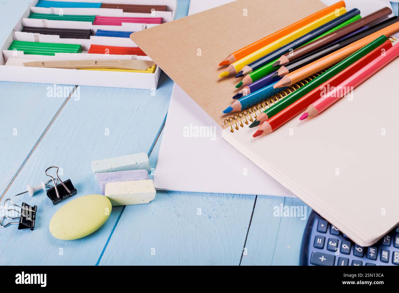 Colorful art supplies arranged on a blue table with a notepad and ...