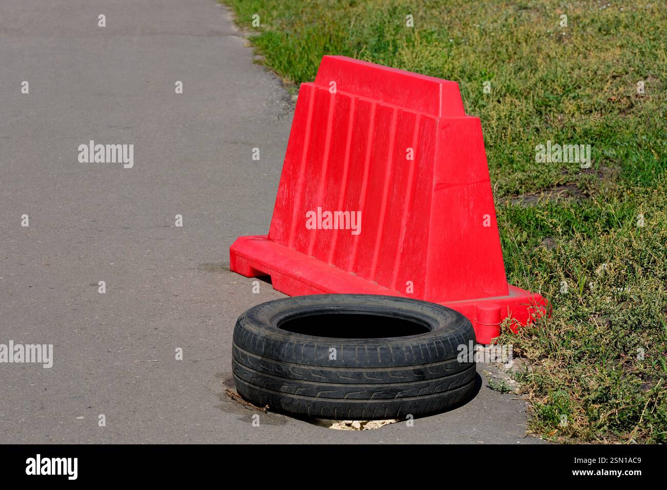 Bright red plastic barrier and black tyre over a hole in the city ...