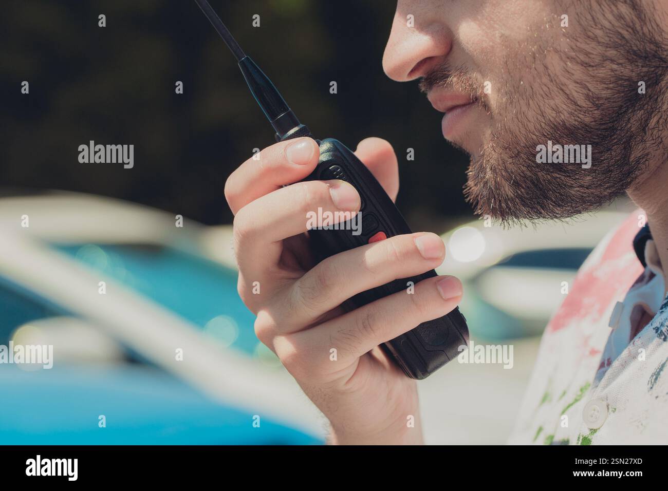 Man using walkie-talkie outdoors at a parking area during daytime ...