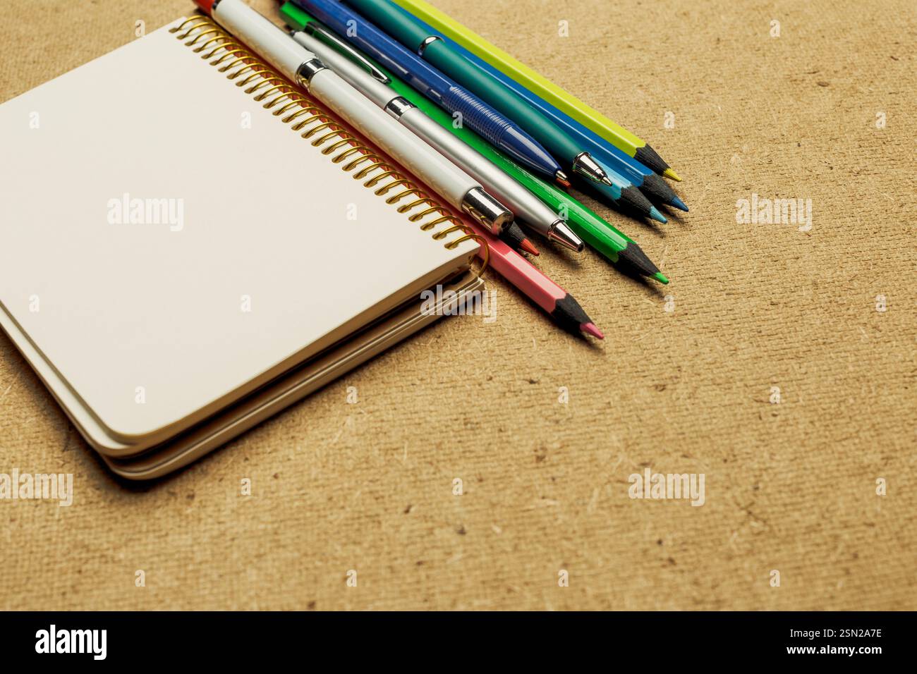 Notepad and colored writing instruments arranged on a textured surface ...