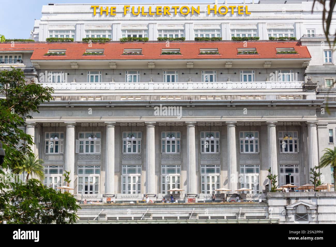 The Fullerton Hotel, guests relax by the swimming pool. Neoclassical architecture design. Day ...