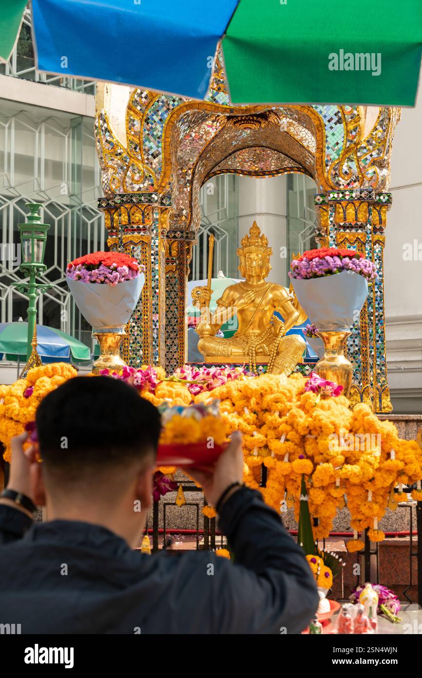 A man can be seen offering prayers at the Erawan Shrine in Bangkok ...