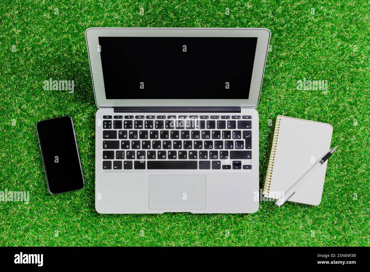 Laptop, smartphone, notepad, and pen arranged on artificial grass ...