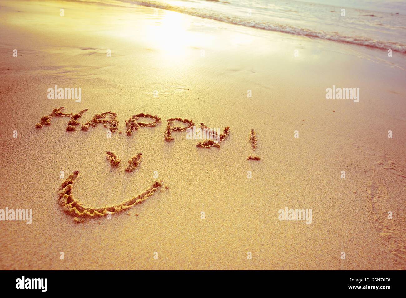 Happy message written in sand by the shoreline during sunset at the ...