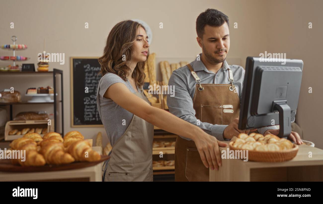 Bakers, man, and woman working together inside a bakery, looking at a ...