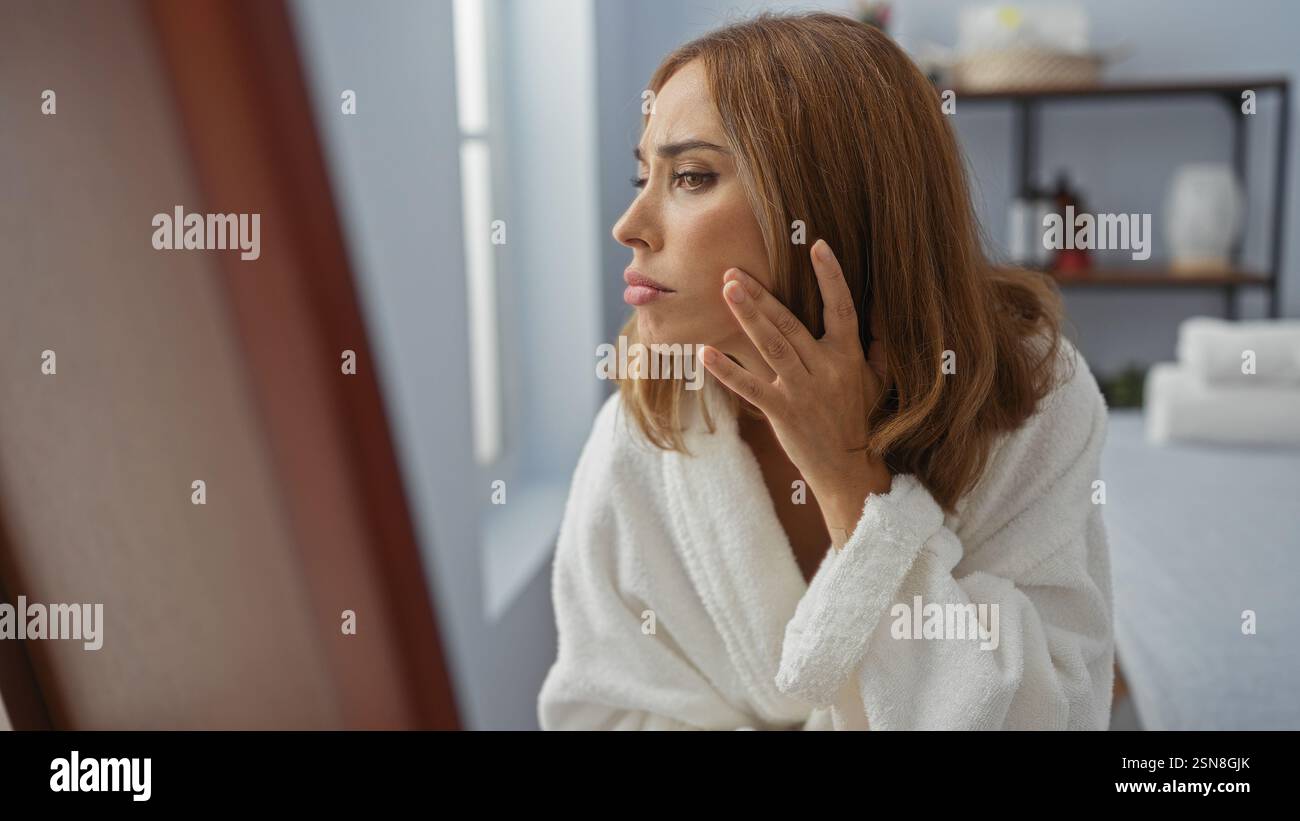 Woman examining skin in mirror at spa in wellness center room wearing ...