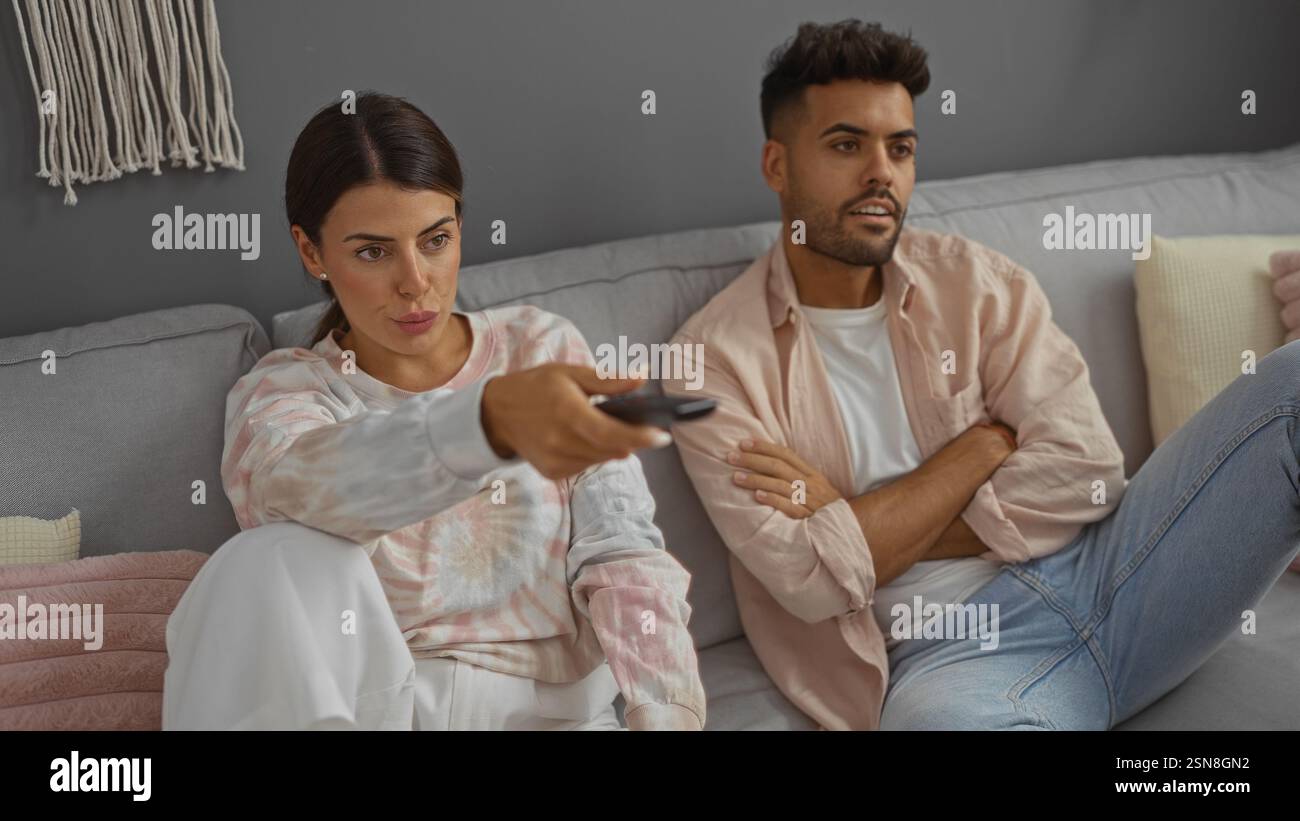Woman pointing remote while man sits next to her on sofa in modern ...