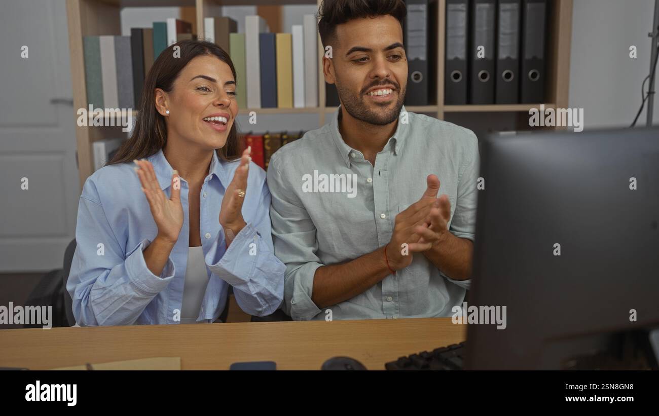 Man and woman work together in an office, clapping in front of a ...