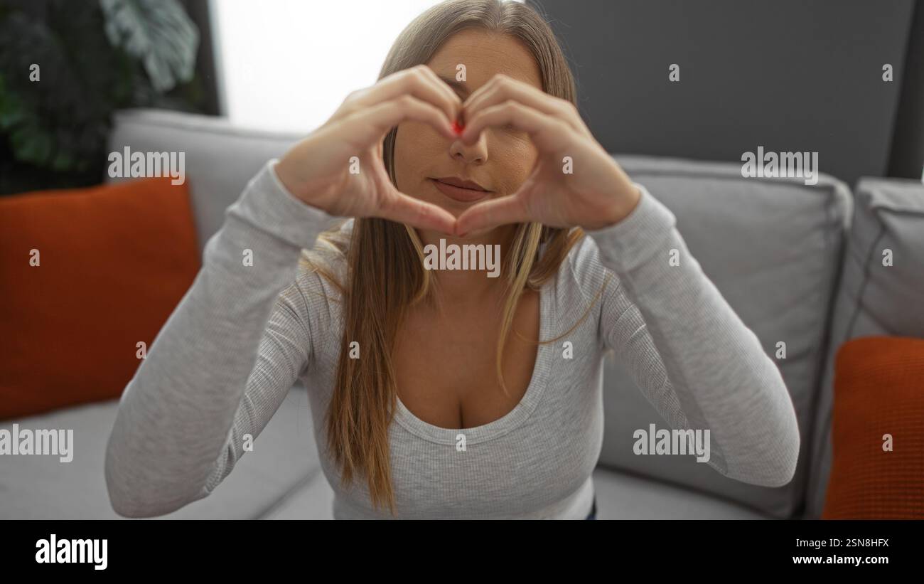 Woman forming heart shape with hands while sitting on a couch in a cozy ...