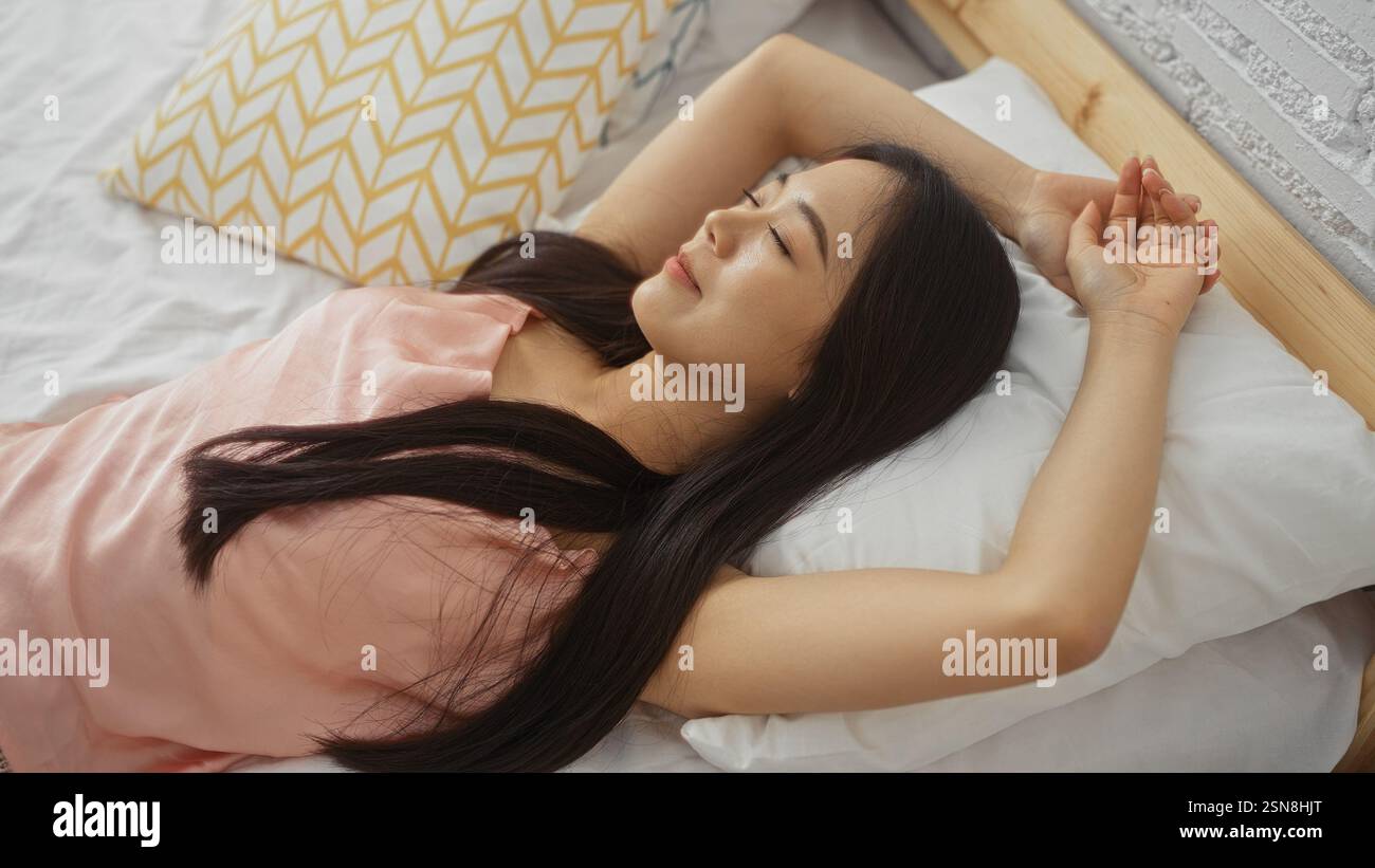 Young chinese woman relaxing in a bedroom lying on a bed, creating an ambiance of calm and ...