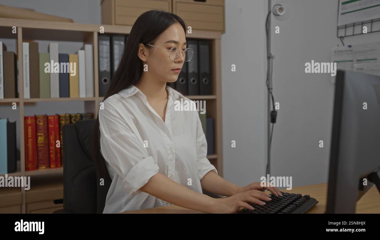 Young chinese woman working on a computer in a tidy office with ...