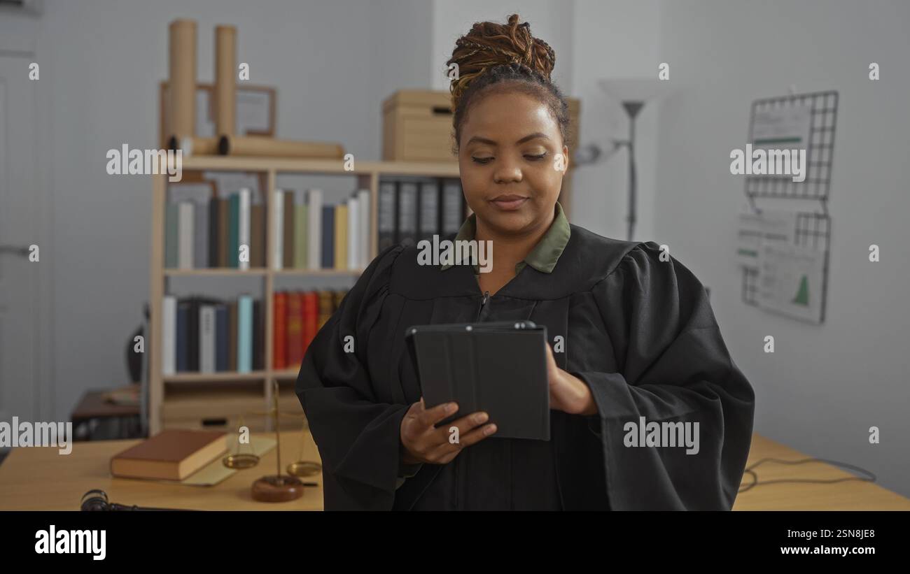 Woman in judge robe standing in office using tablet with bookshelf and ...