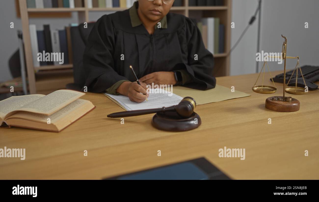 Woman judge writing notes at desk in courtroom with law books, gavel ...