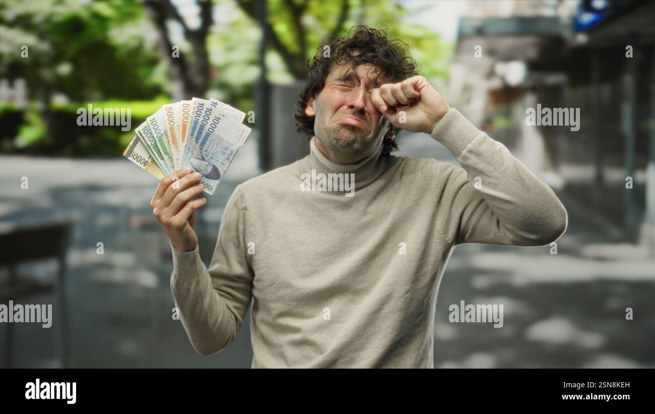 Hispanic man crying while holding south korean banknotes outdoors on a ...
