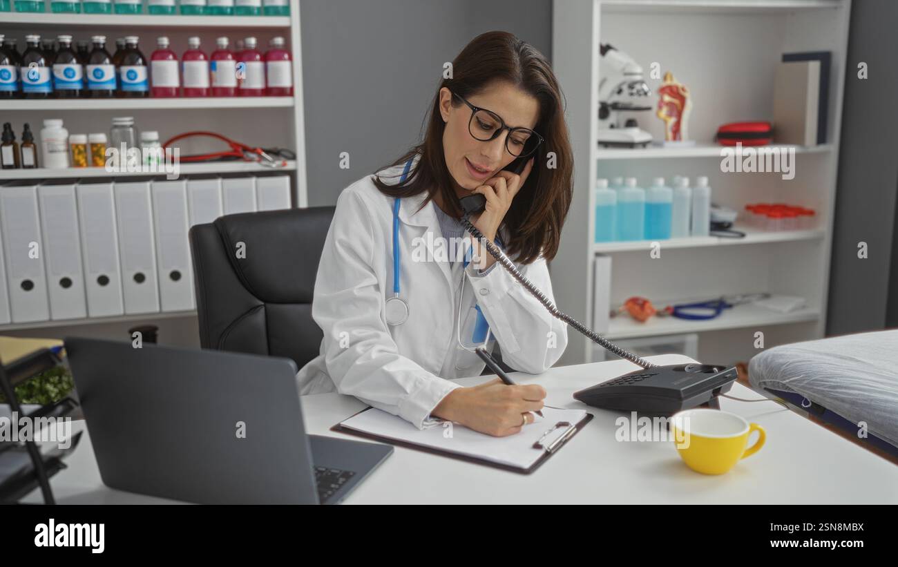 Woman doctor talking on phone while writing notes in a clinic office ...