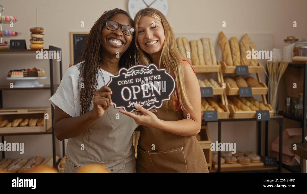 Smiling bakers women holding open sign in bakery shop filled with bread ...