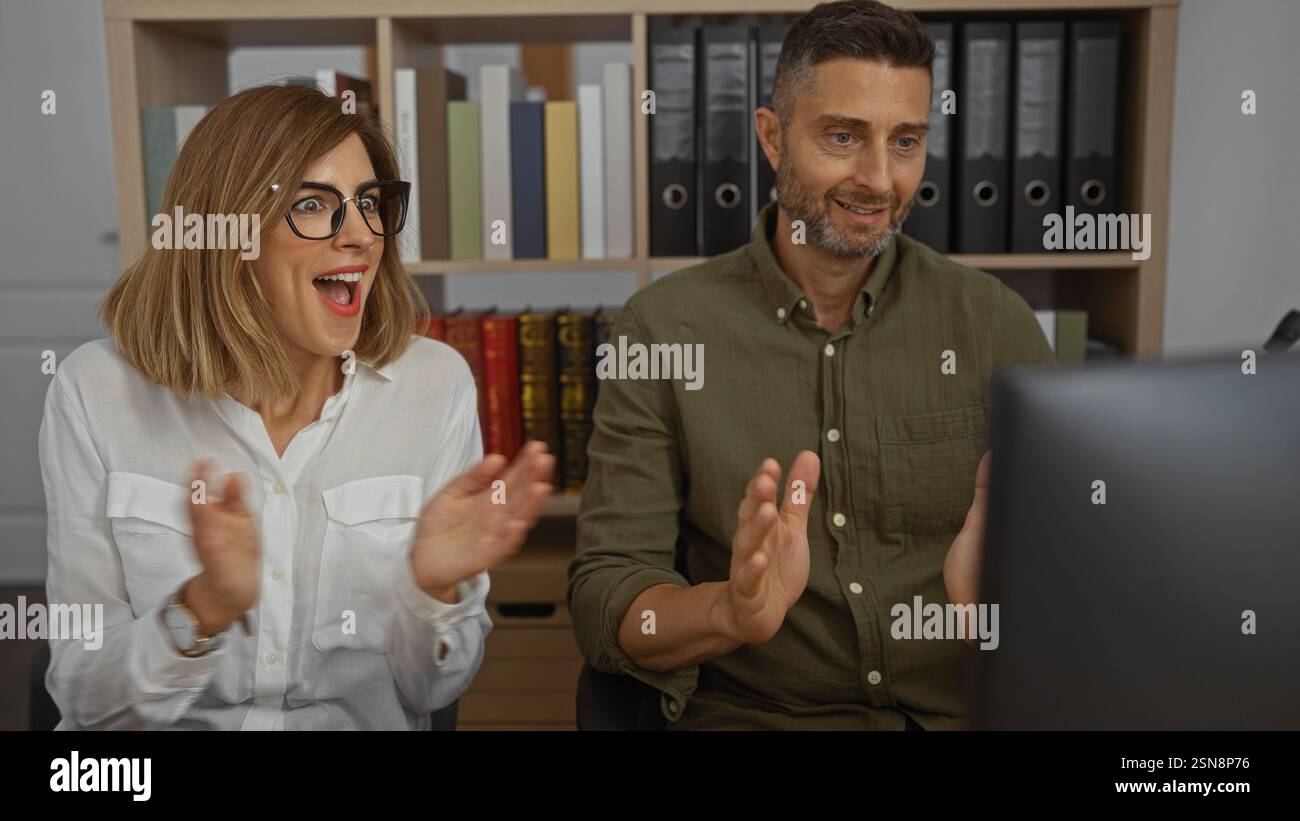 Man and woman applauding together in an office setting, surrounded by ...