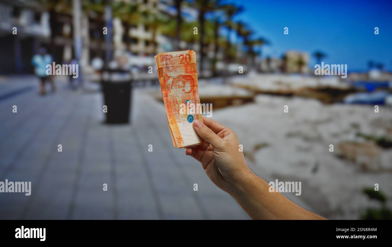 Hand holding philippine 20 peso banknote in a sunny seaside town street ...