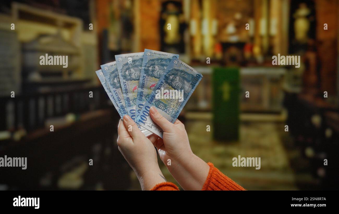 Woman holding hungarian forint banknotes inside a church, highlighting ...