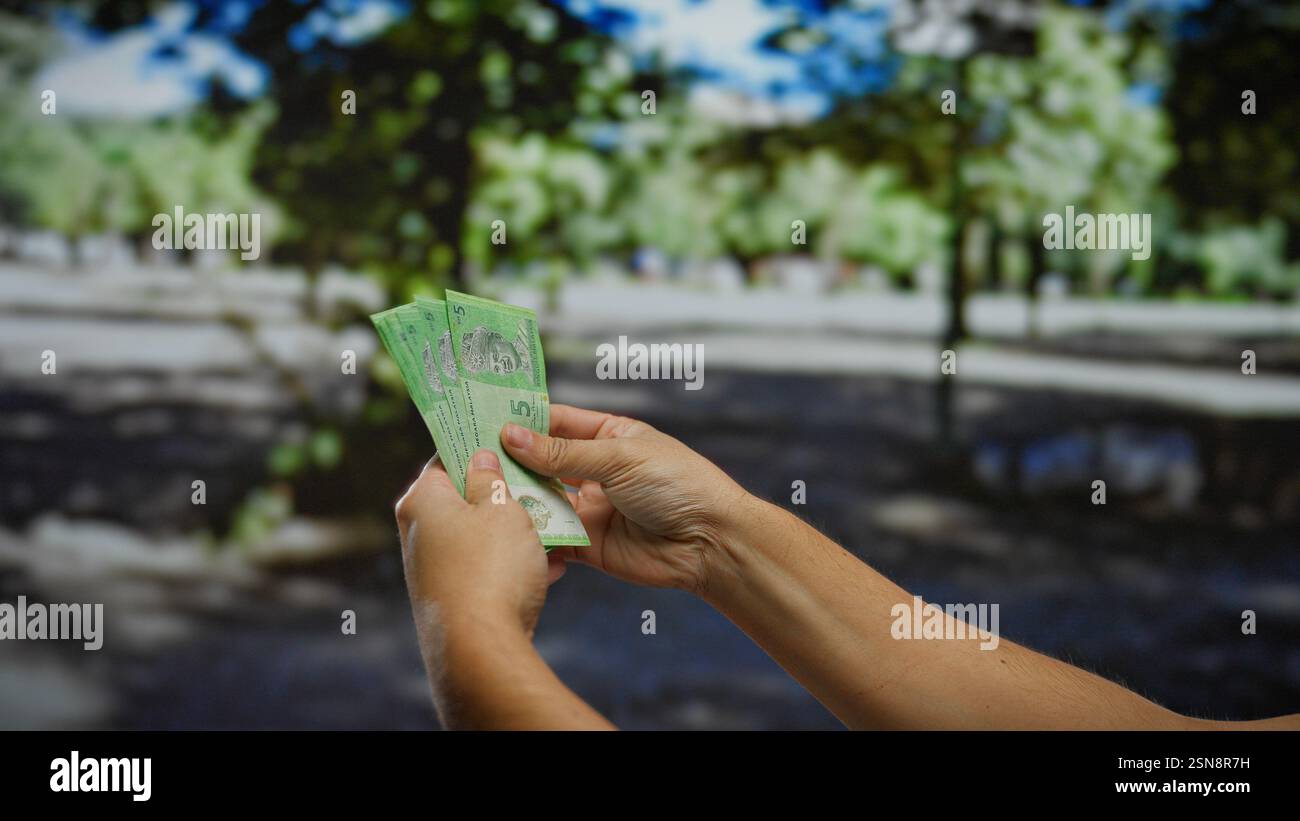 Man holding malaysian banknotes in a city park setting, highlighting ...