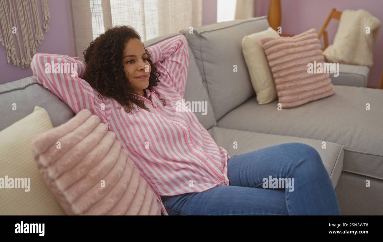 Young woman with curly hair relaxing on a sofa in the living room of ...