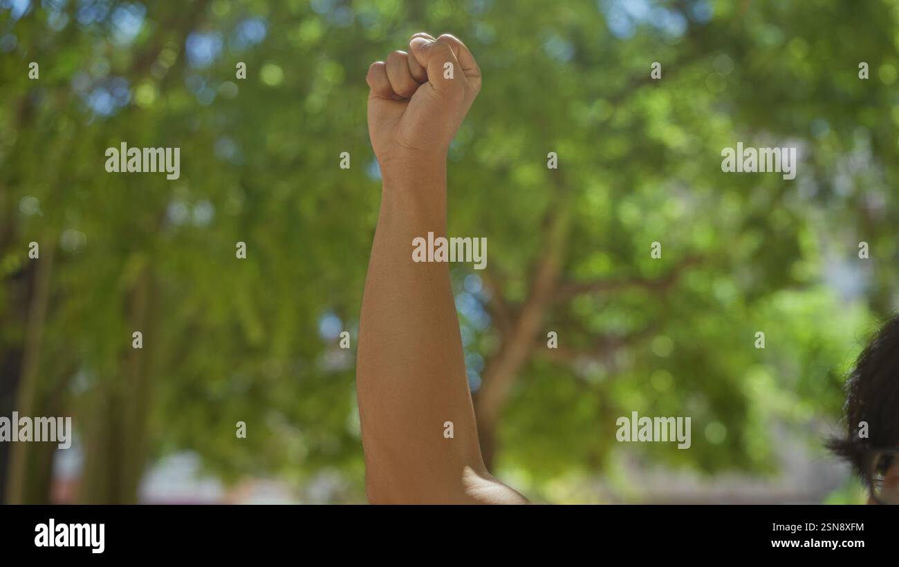 Young man raising fist in an outdoor urban park showing determination ...