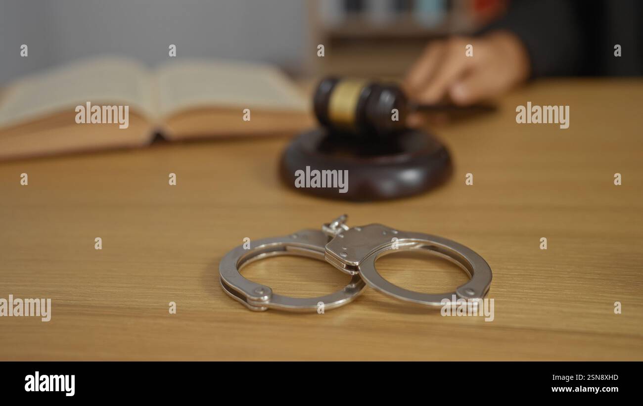 Handcuffs on desk in courtroom, with judge's gavel and books in ...