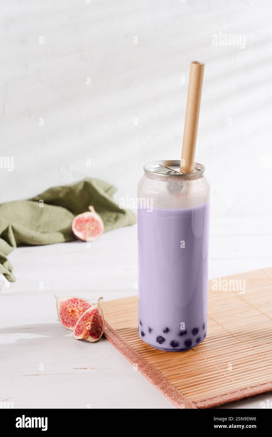 A purple bubble tea with boba pearls in a to-go cup with paper straw ...