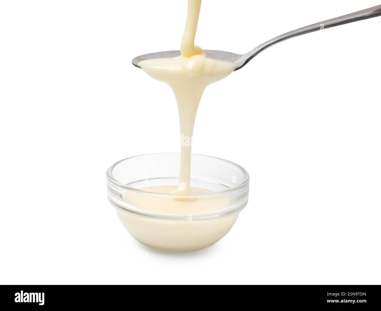 Condensed milk flowing down from spoon into bowl isolated on white ...