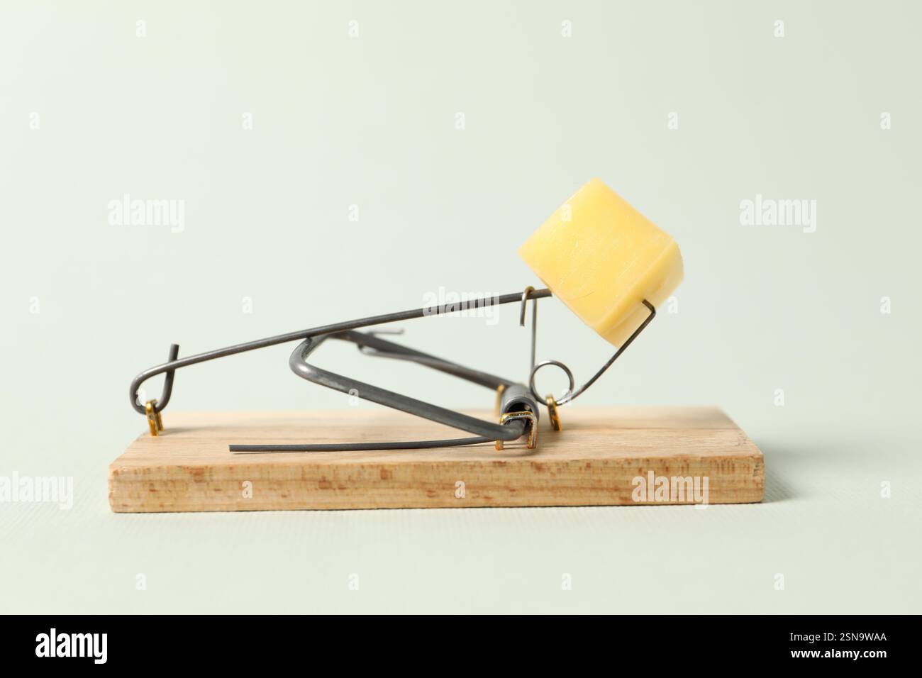 Spring-loaded bar mousetrap with piece of cheese on light background ...