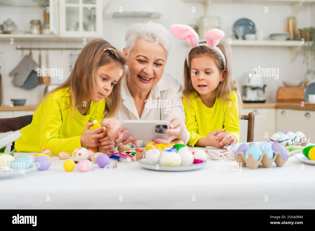 Happy Easter. Two girls sisters twins grandmother painting eggs ...