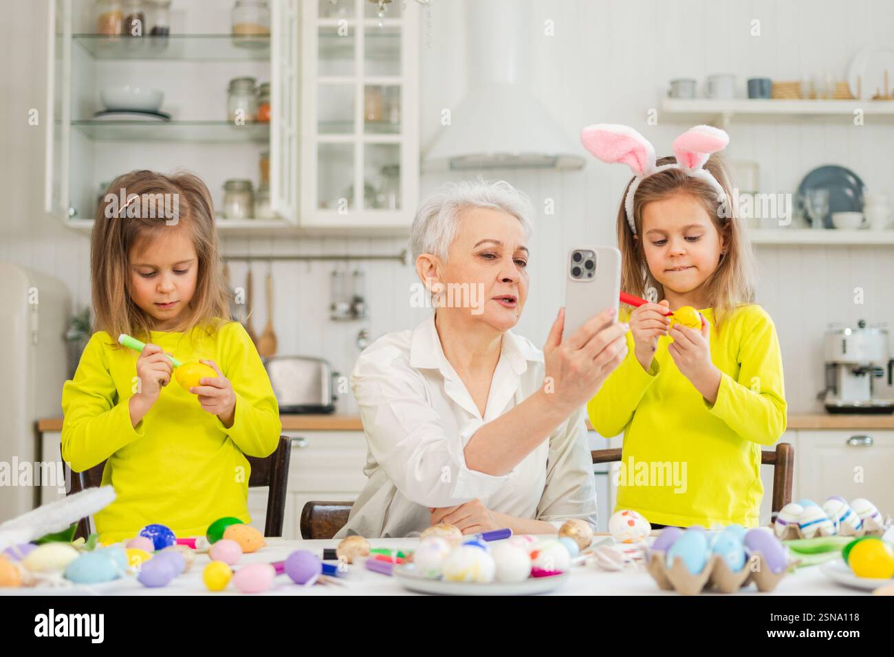 Happy Easter. Two girls sisters grandmother painting eggs having video ...