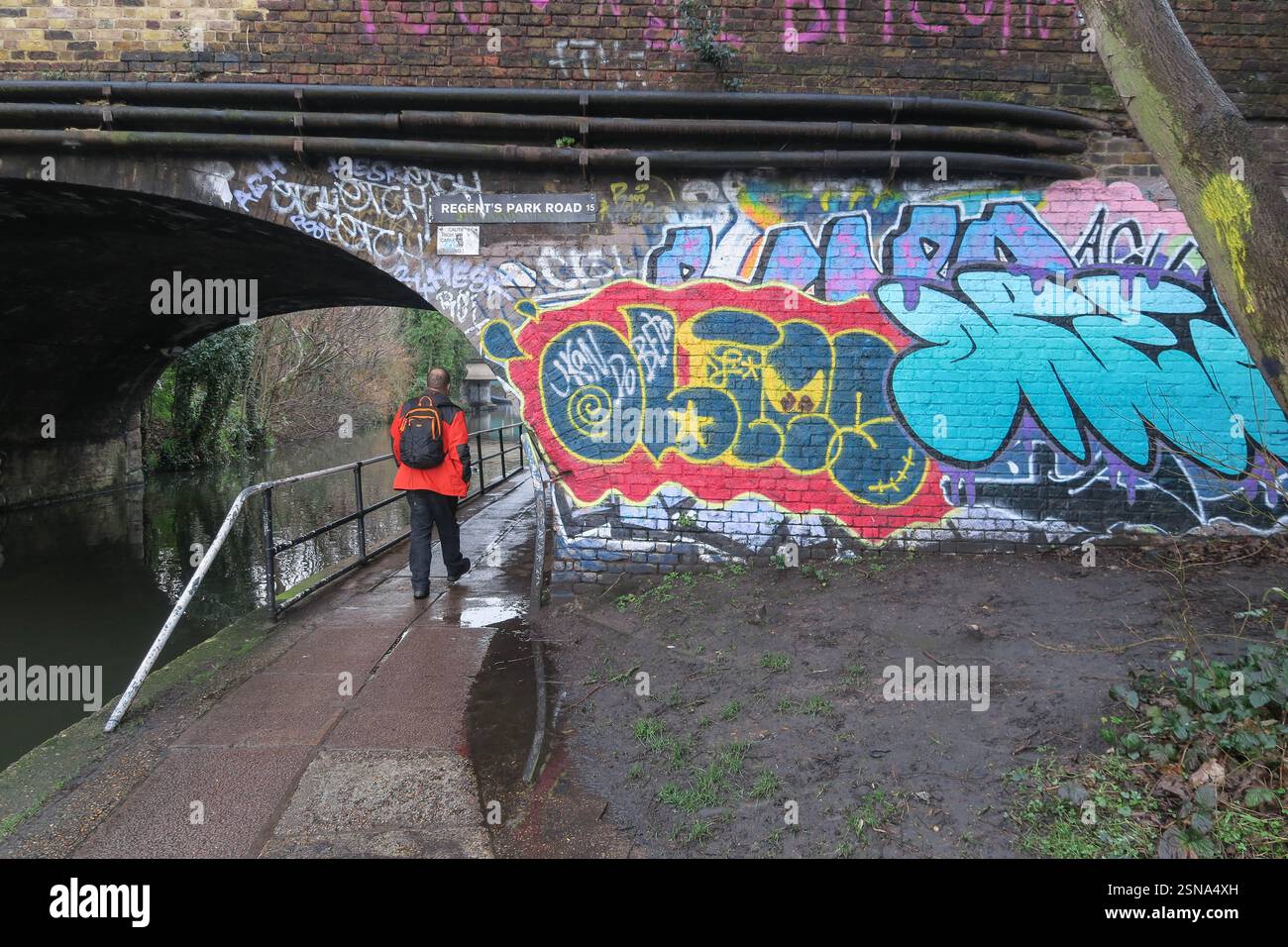 Man walking under a bridge covered with graffiti, at Regents Park Road ...