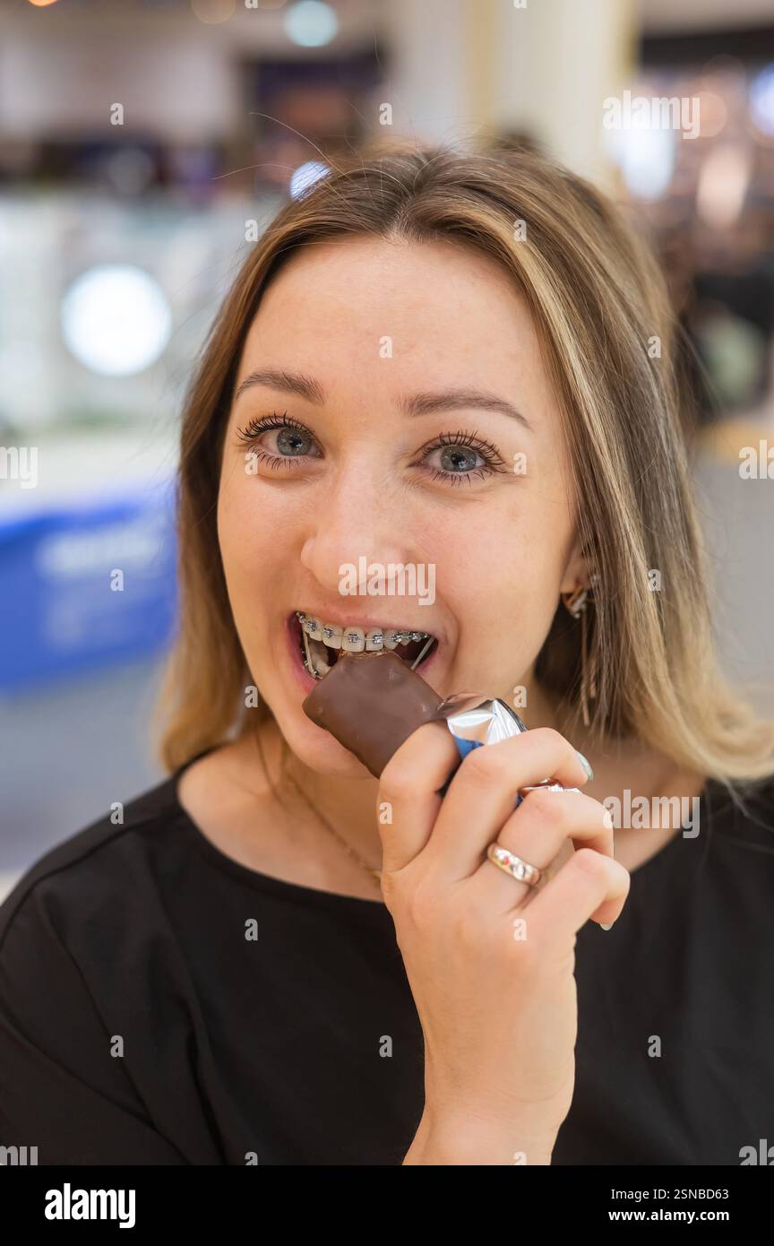 Portrait of a woman with braces on her teeth eating a chocolate bar ...