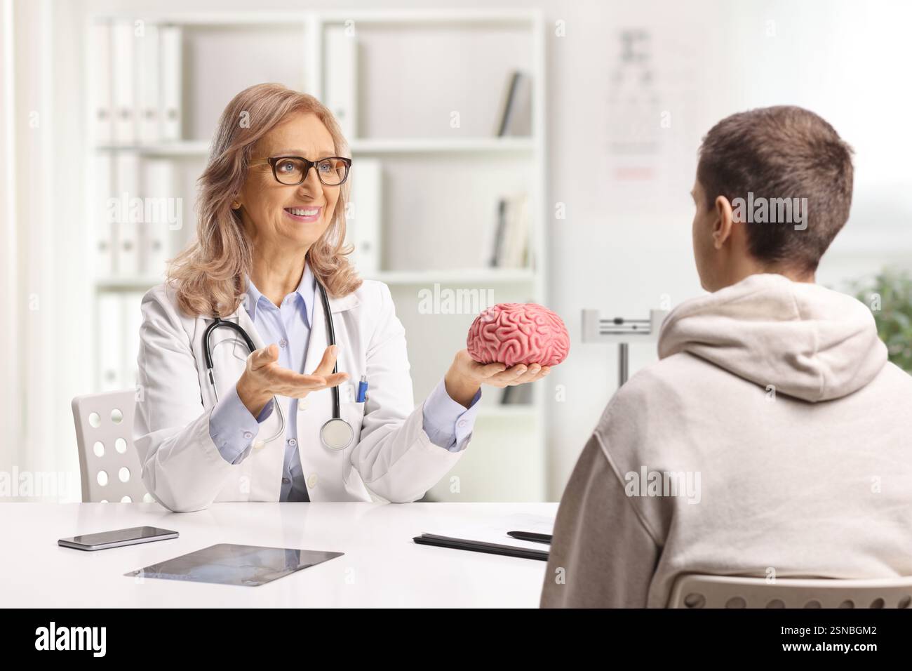 Female doctor sitting with a patient and holding a brain model at the ...