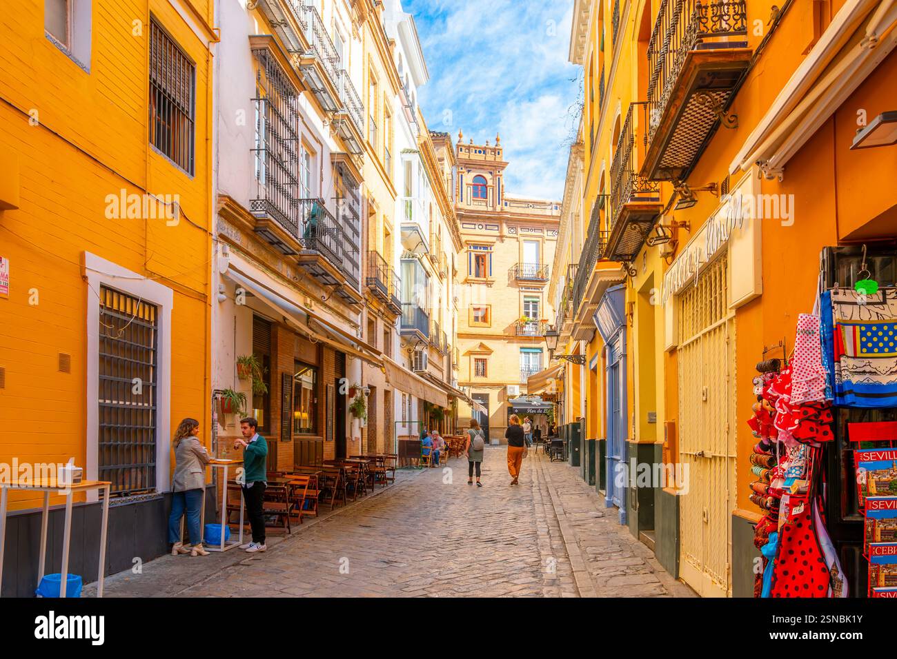 Pedestrians walk past shops and sidewalk cafes through a narrow ...