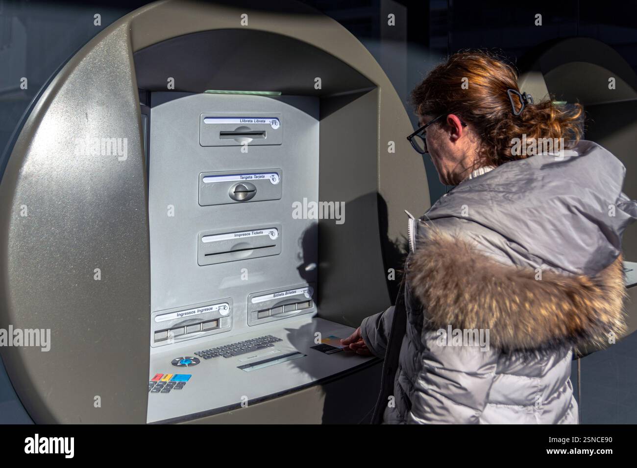 Woman performing a transaction at an outdoor ATM in winter clothing ...