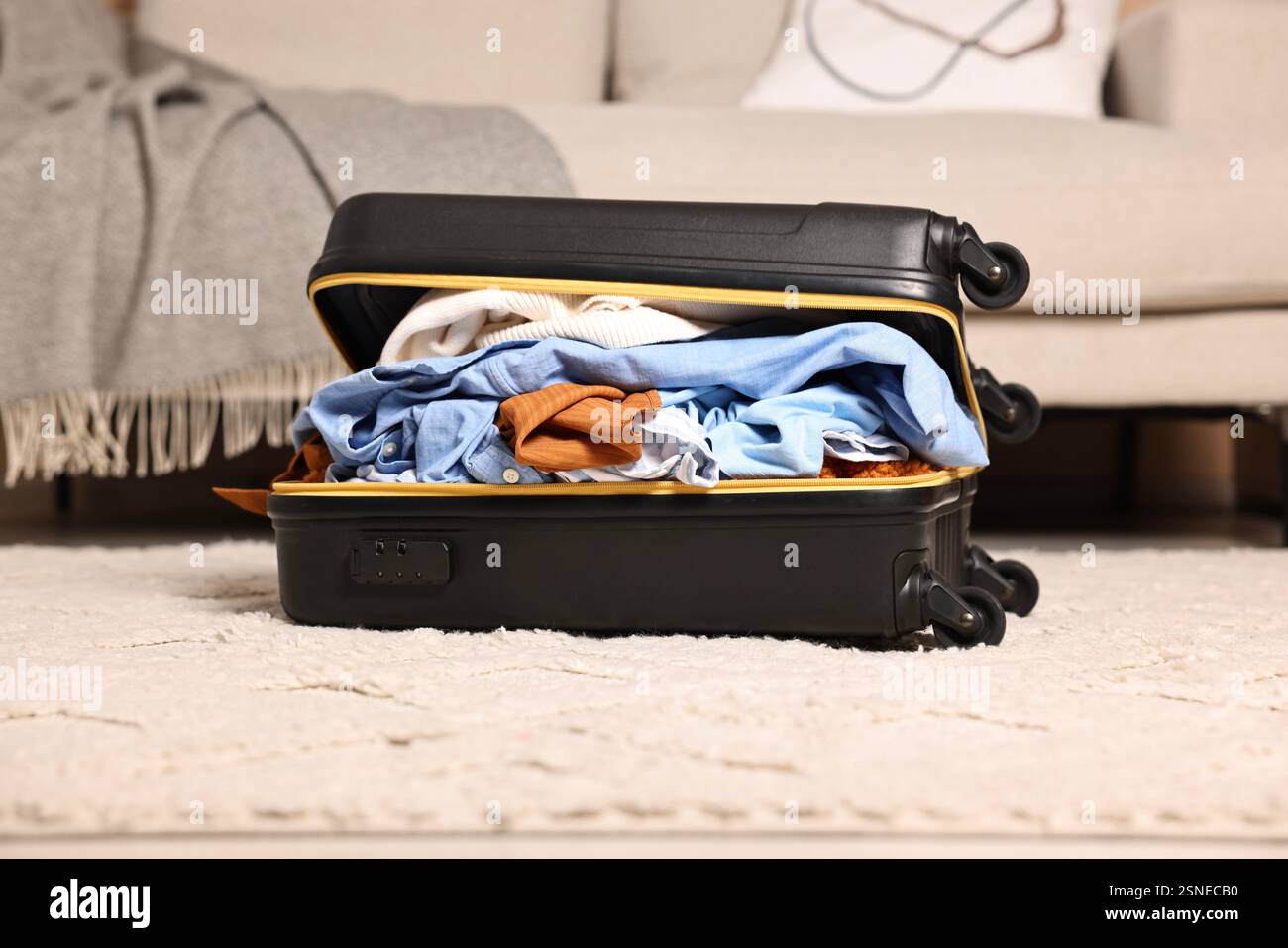 Open suitcase full of different messy clothes on floor indoors Stock ...