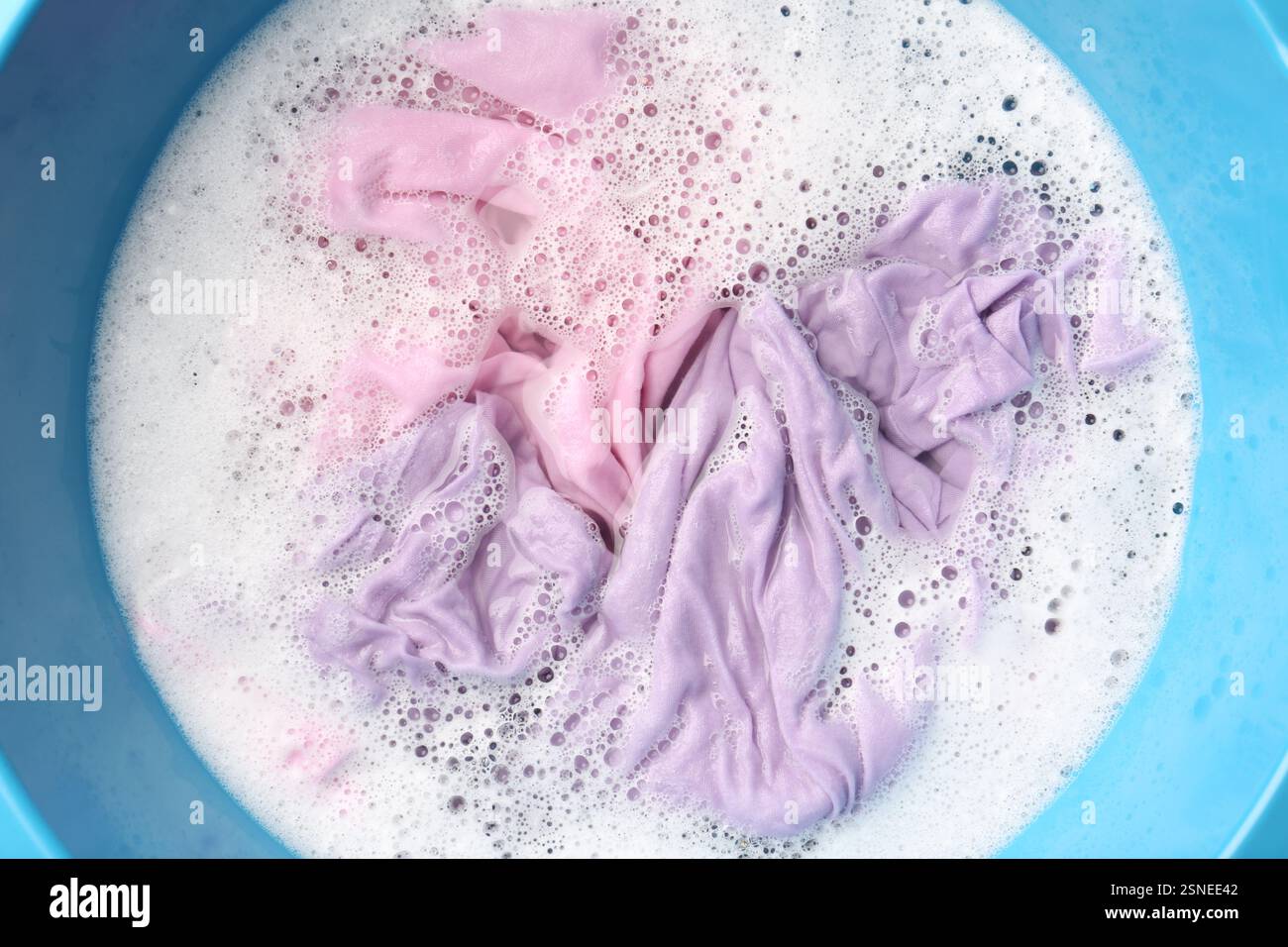 Colorful clothes soaked in water before washing, top view Stock Photo ...