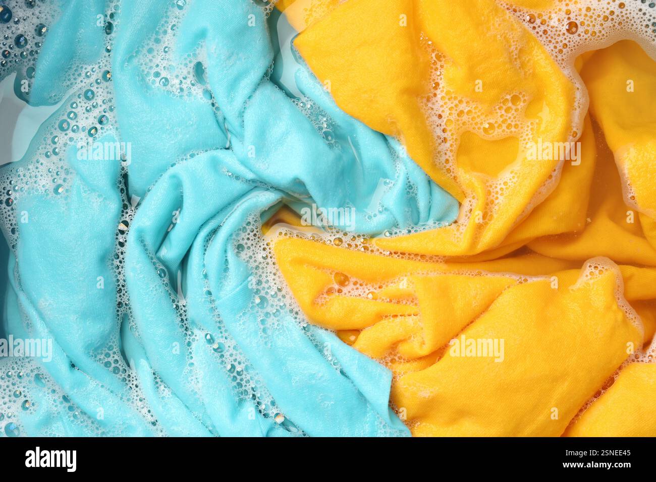 Colorful clothes soaked in water before washing, top view Stock Photo ...